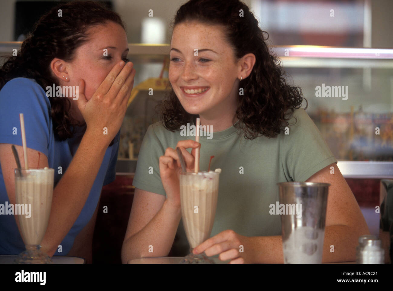 Two teenage twin girls sitting in a restaurant with malts in front of ...
