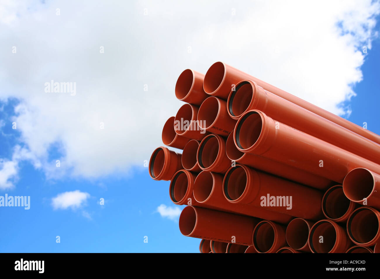 Stacked orange PVC pipes against a blue sky with clouds Stock Photo - Alamy
