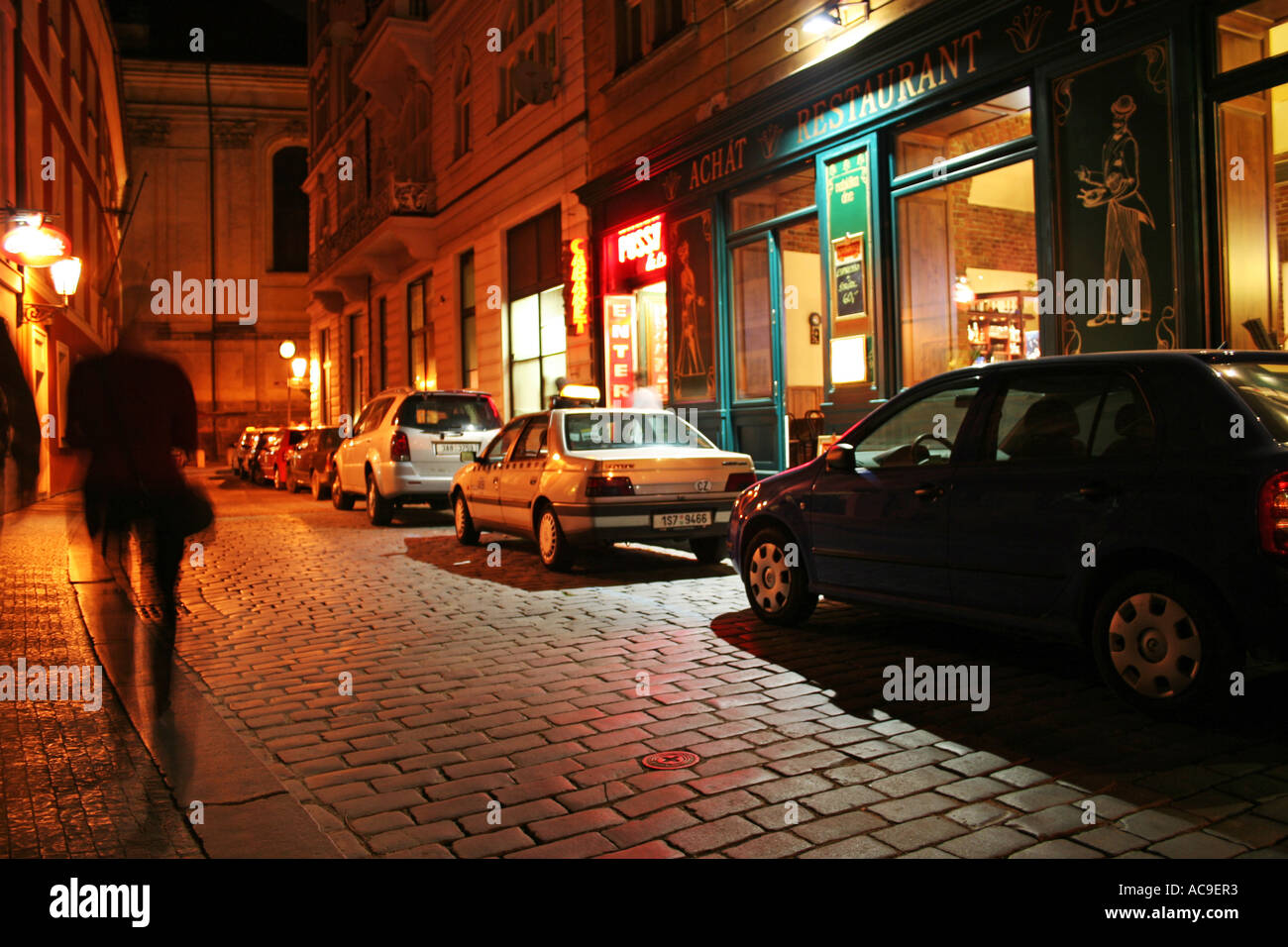 Prague street at night with parked cars, illuminated restaurant, and a ...