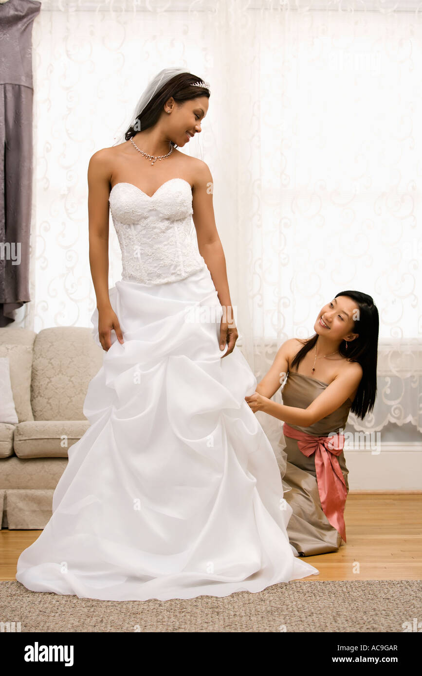 Asian bridesmaid fixing African American bride s dress Stock Photo - Alamy