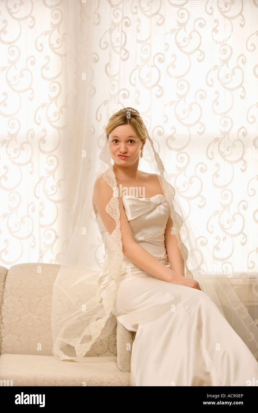 Portrait of Caucasian bride sitting on love seat making a funny ...