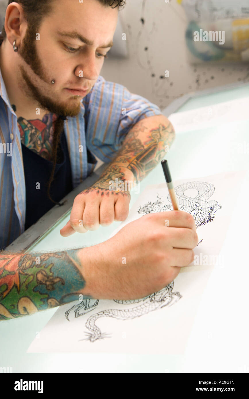 Caucasian male tattoo artist drawing tattoo on light table Stock Photo ...