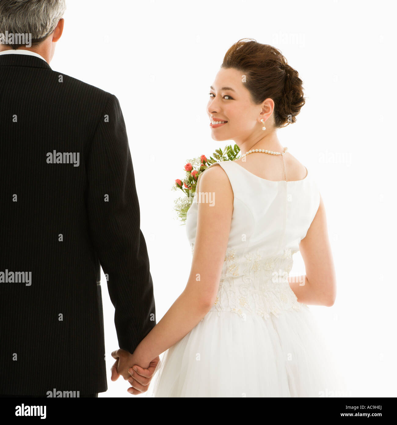 Asian bride looking over her shoulder while holding Caucasian groom s ...