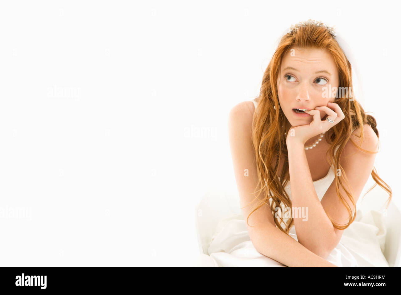 Portrait of sitting Caucasian bride biting her finger and looking off ...