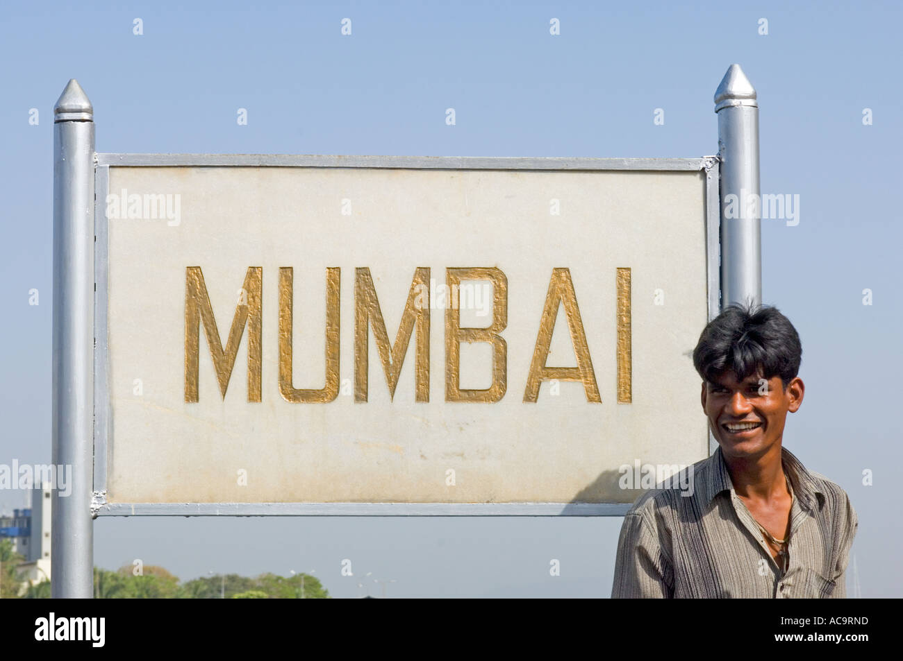 A local Indian man smiling standing by a Mumbai sign near the Gateway ...