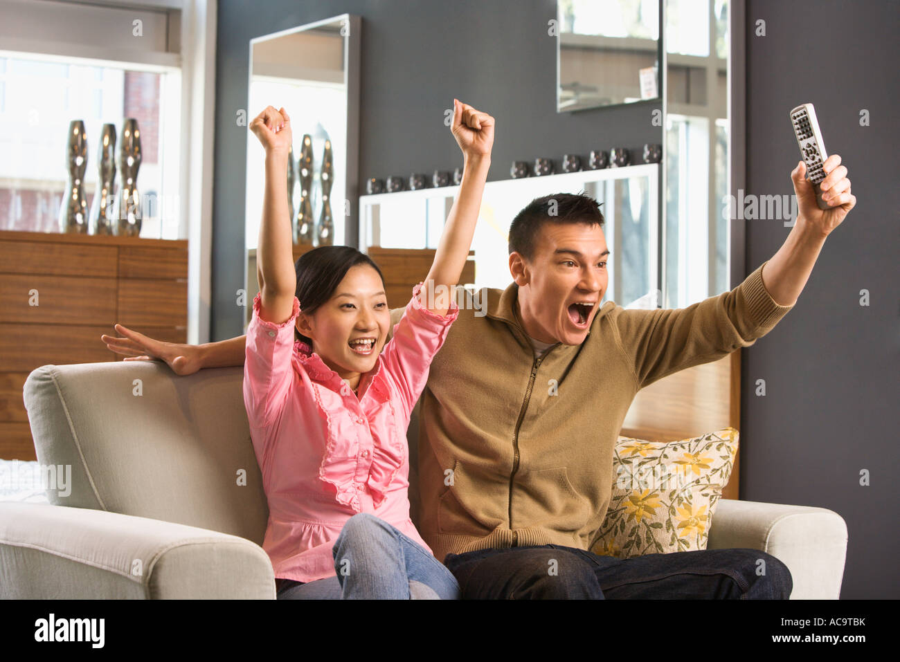 Asian couple cheering while watching television Stock Photo - Alamy