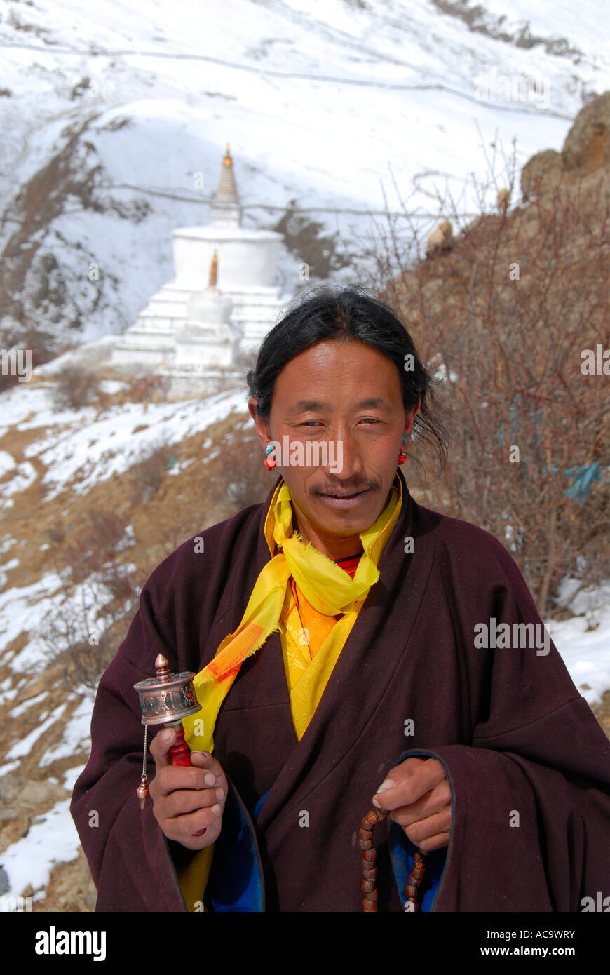 Tibetan pilgrim at kora with prayer wheel in front of stupa in the snow ...