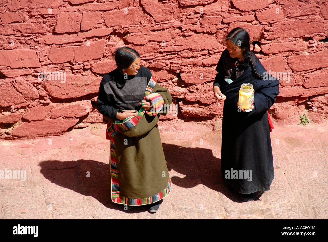 Tibetan women stand at red painted wall Ganden Monastery Tibet China ...