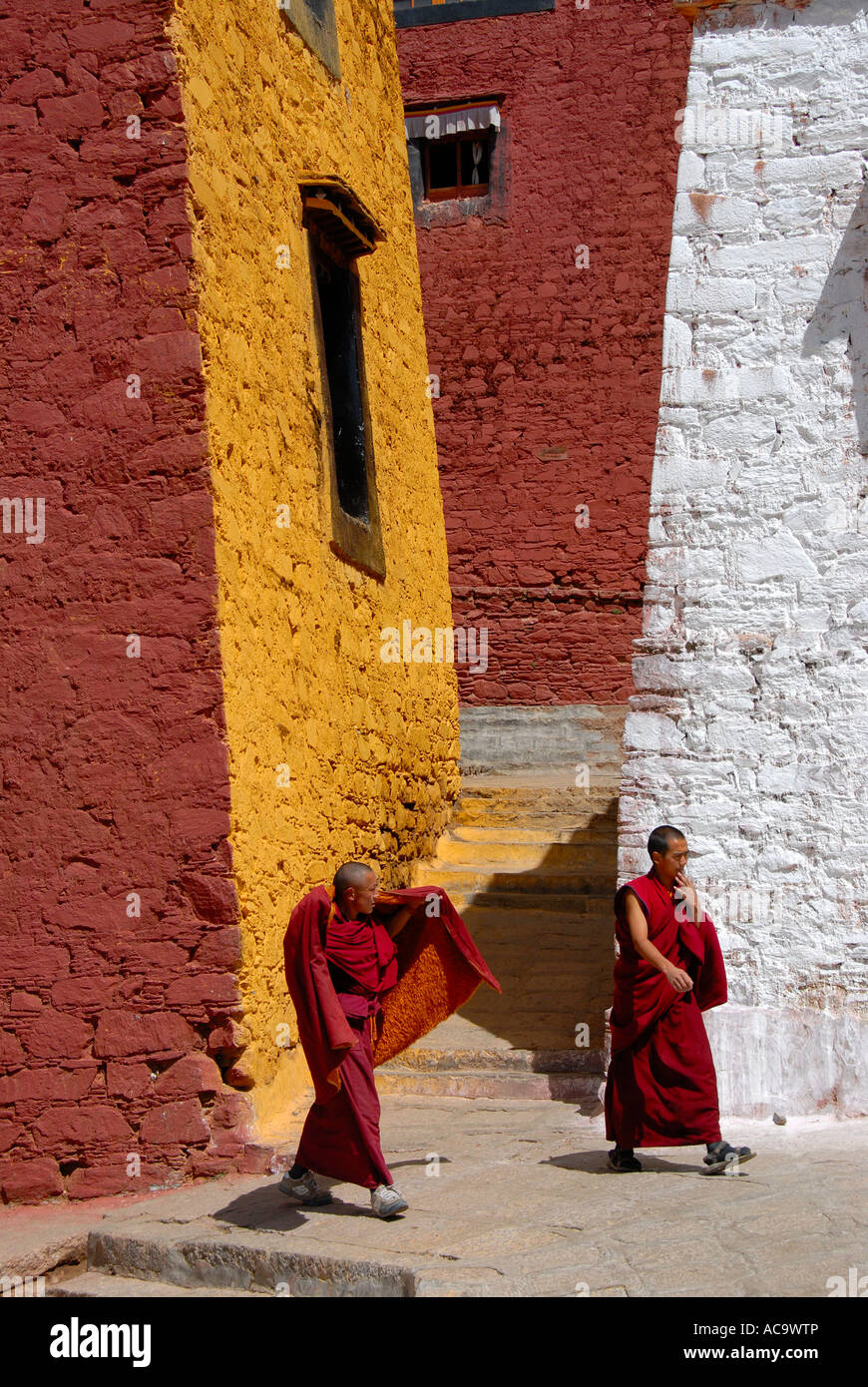 Tibetan monks walk by red ochre and white painted wall Ganden Monastery ...