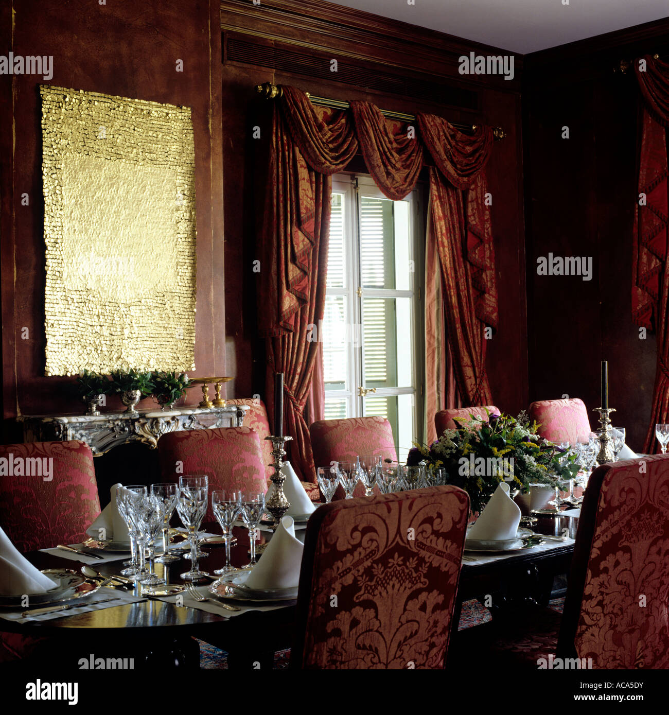 Laid dining table with candles and wine glasses, red upholstered chairs ...