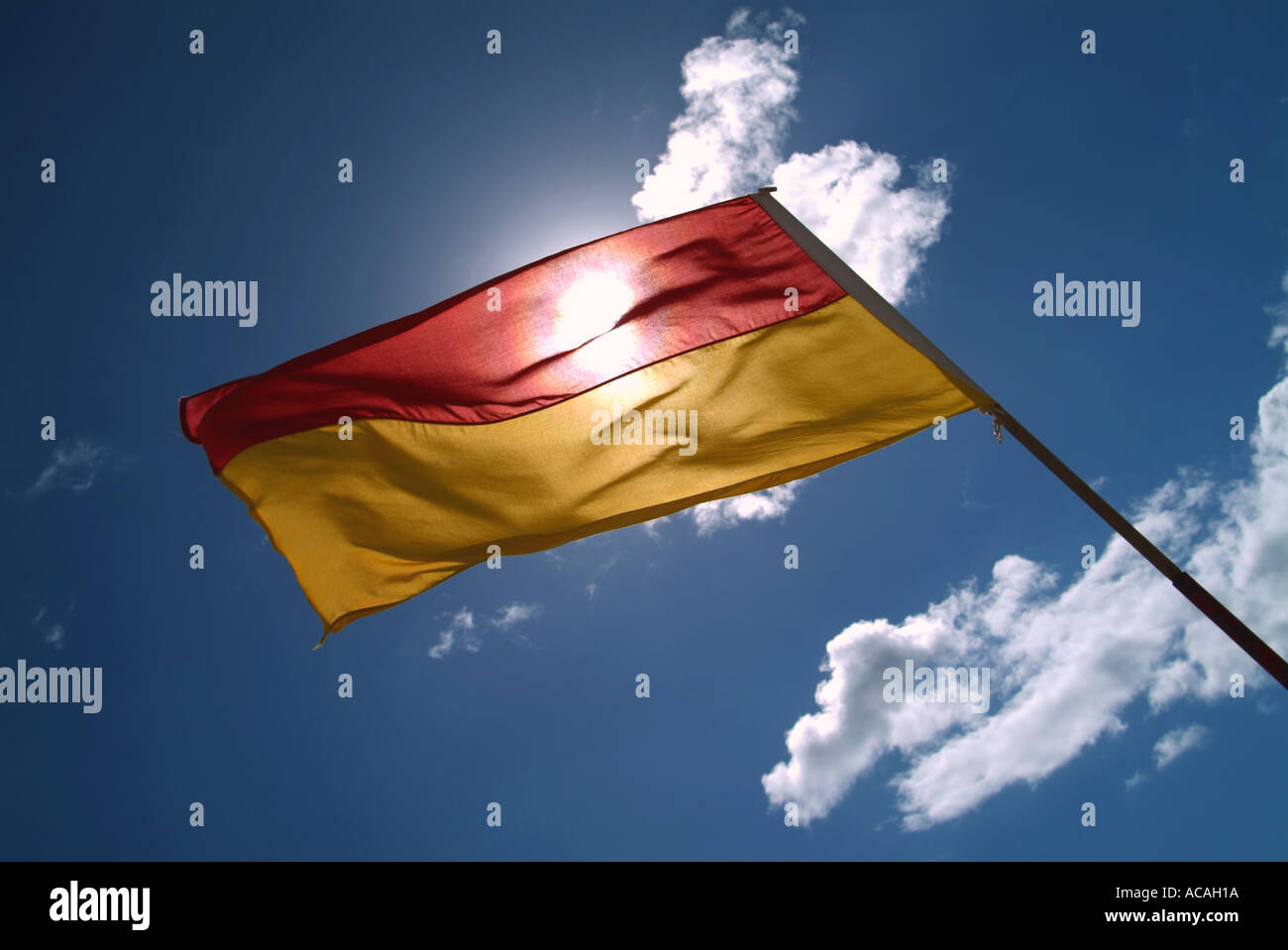 Red and yellow warning flag backlit by the sun against a deep blue sky ...