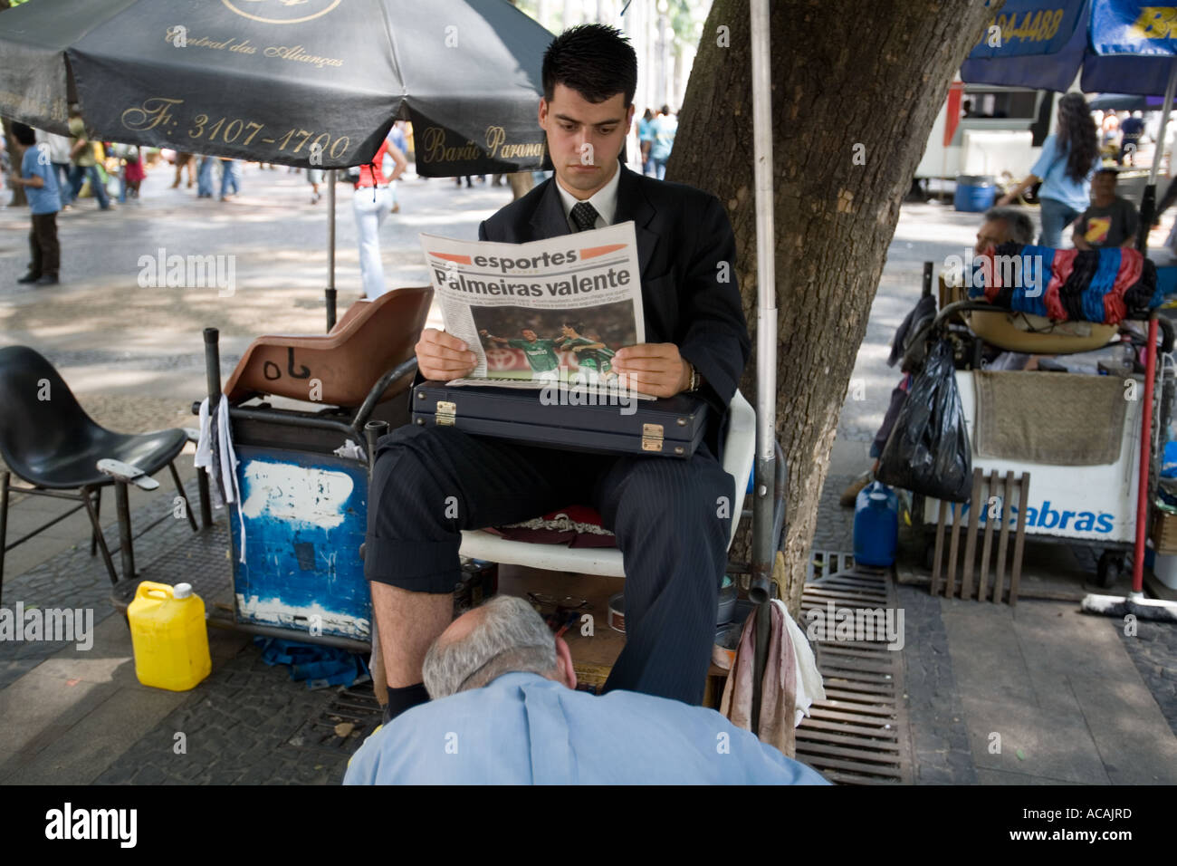 A young man is reading the local newspaper while has his shoes polished ...