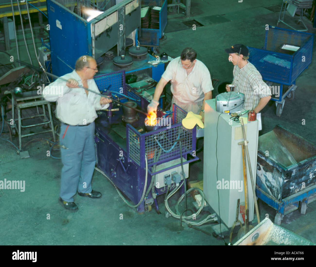 Glass makers at work in a glass factory pouring hot molten glass into ...