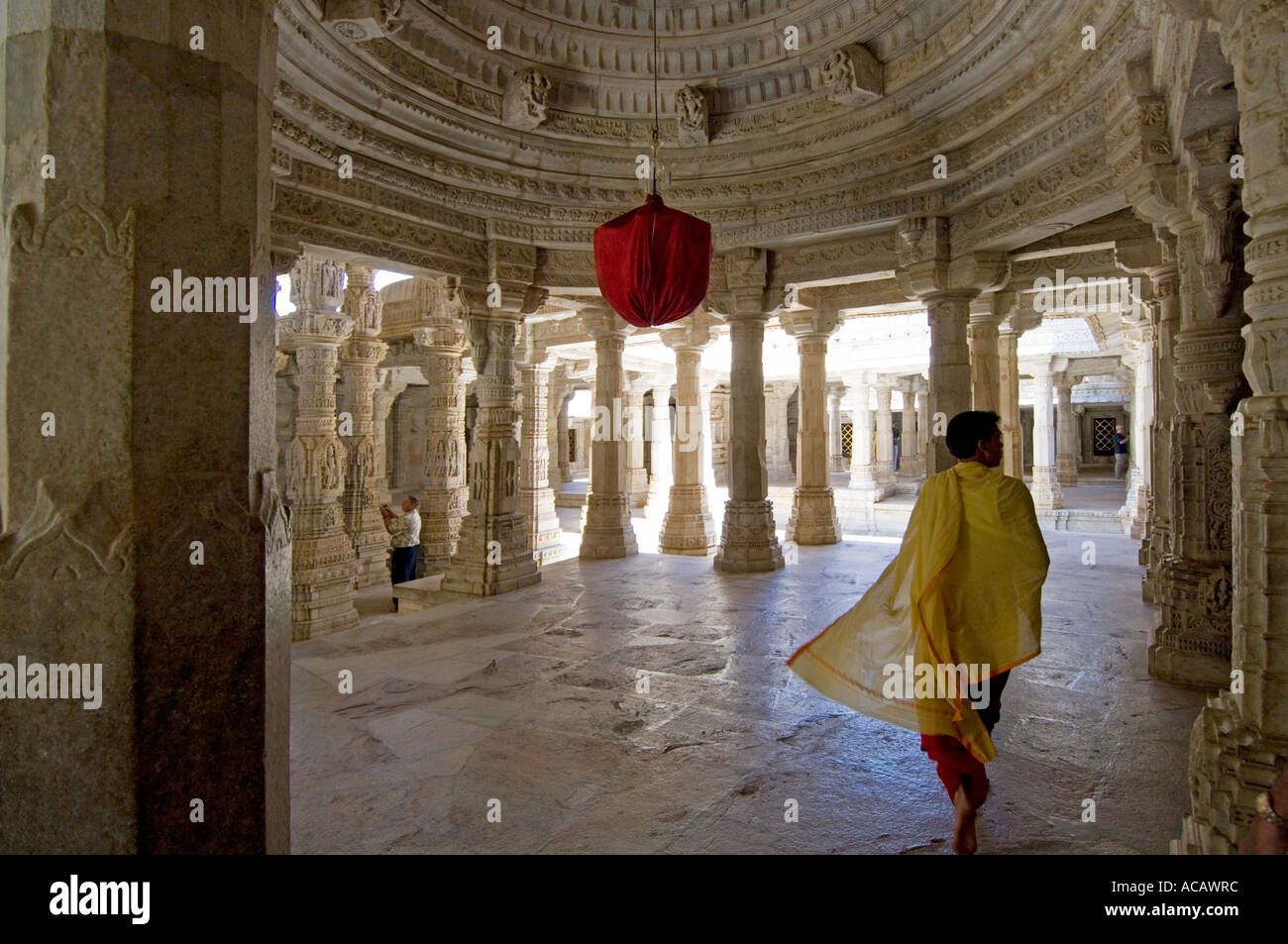 A Jain priest walking through the forest of intricately carved pillars ...