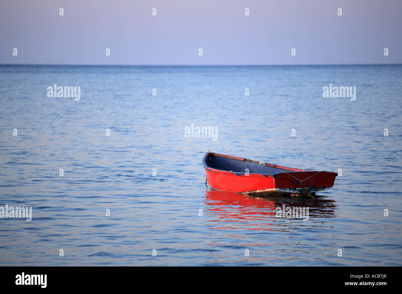 A solitary red rowing boat and its reflection in an otherwise deserted ...