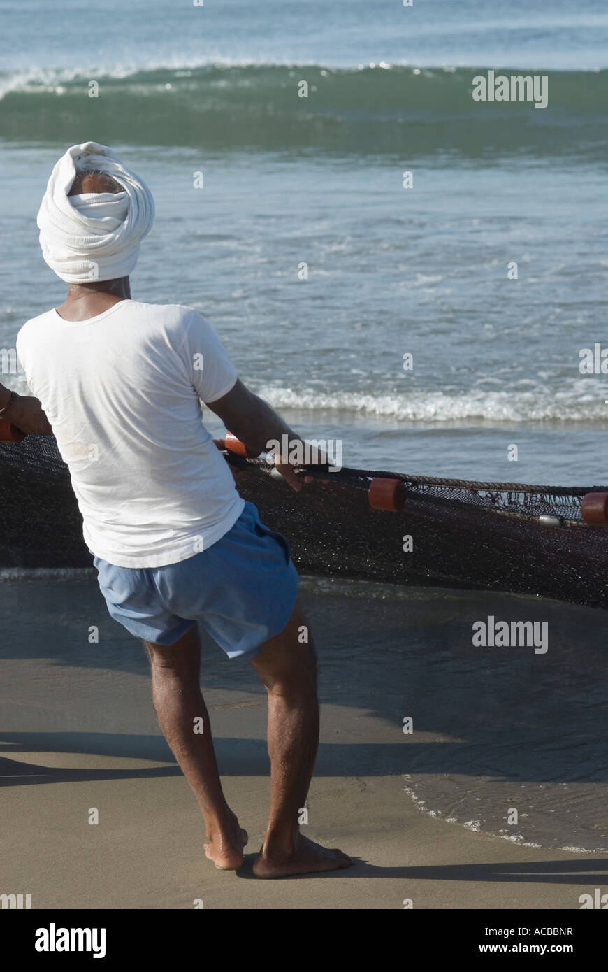 Rear view of a man pulling a fishing net on the beach, Morjim Beach ...