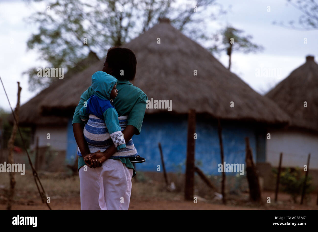 Woman carrying her baby on back, thatched huts in background, Venda ...