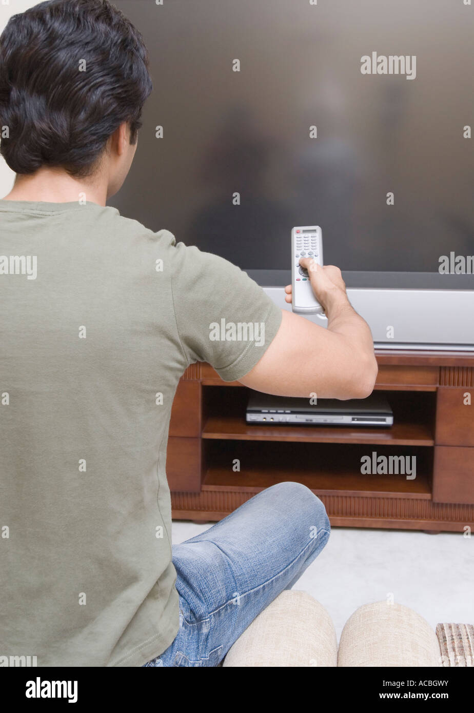 Rear view of a young man sitting on a couch and operating a remote ...