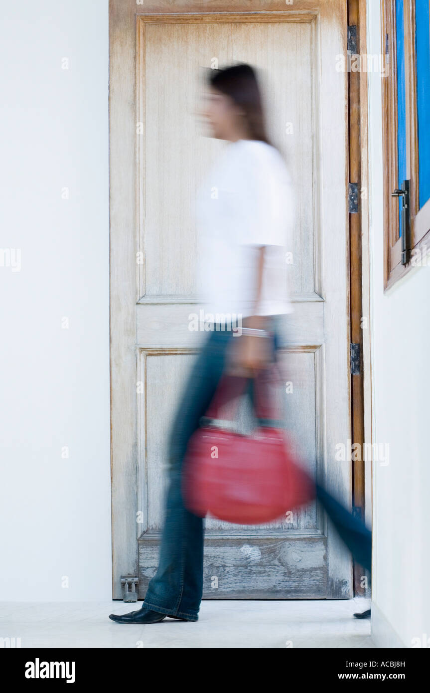 Side profile of a young woman carrying a hand bag and walking out of a ...