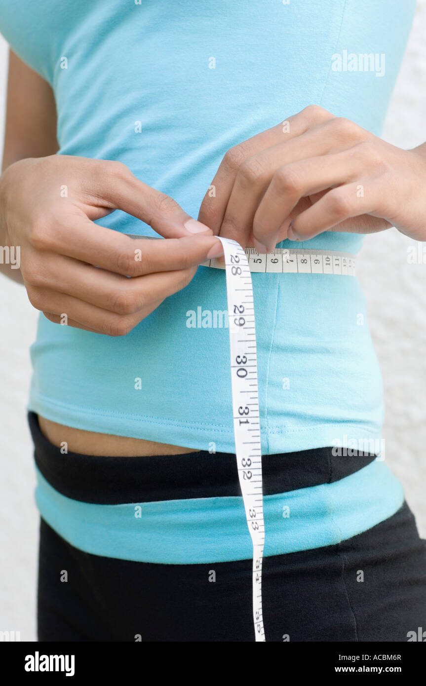 Mid section view of a young woman measuring her waist with a tape ...