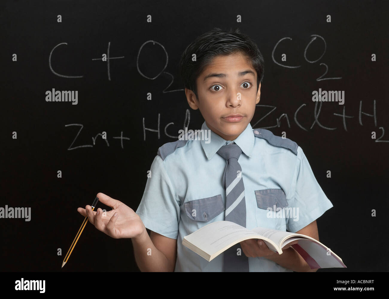Close-up of a boy holding a pencil and a book in front of a blackboard ...