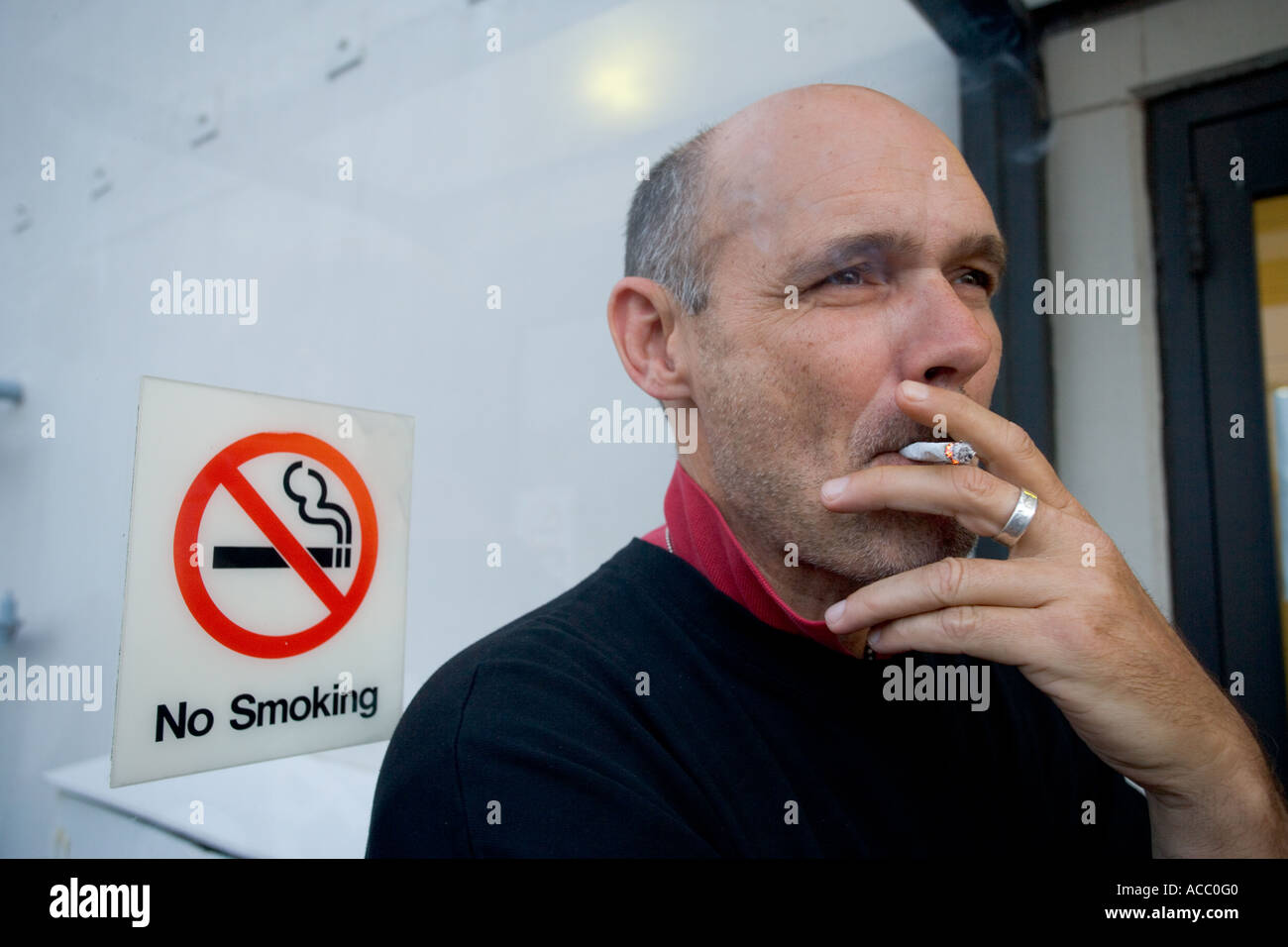 Man smoke in front of non smoking sign Stock Photo - Alamy