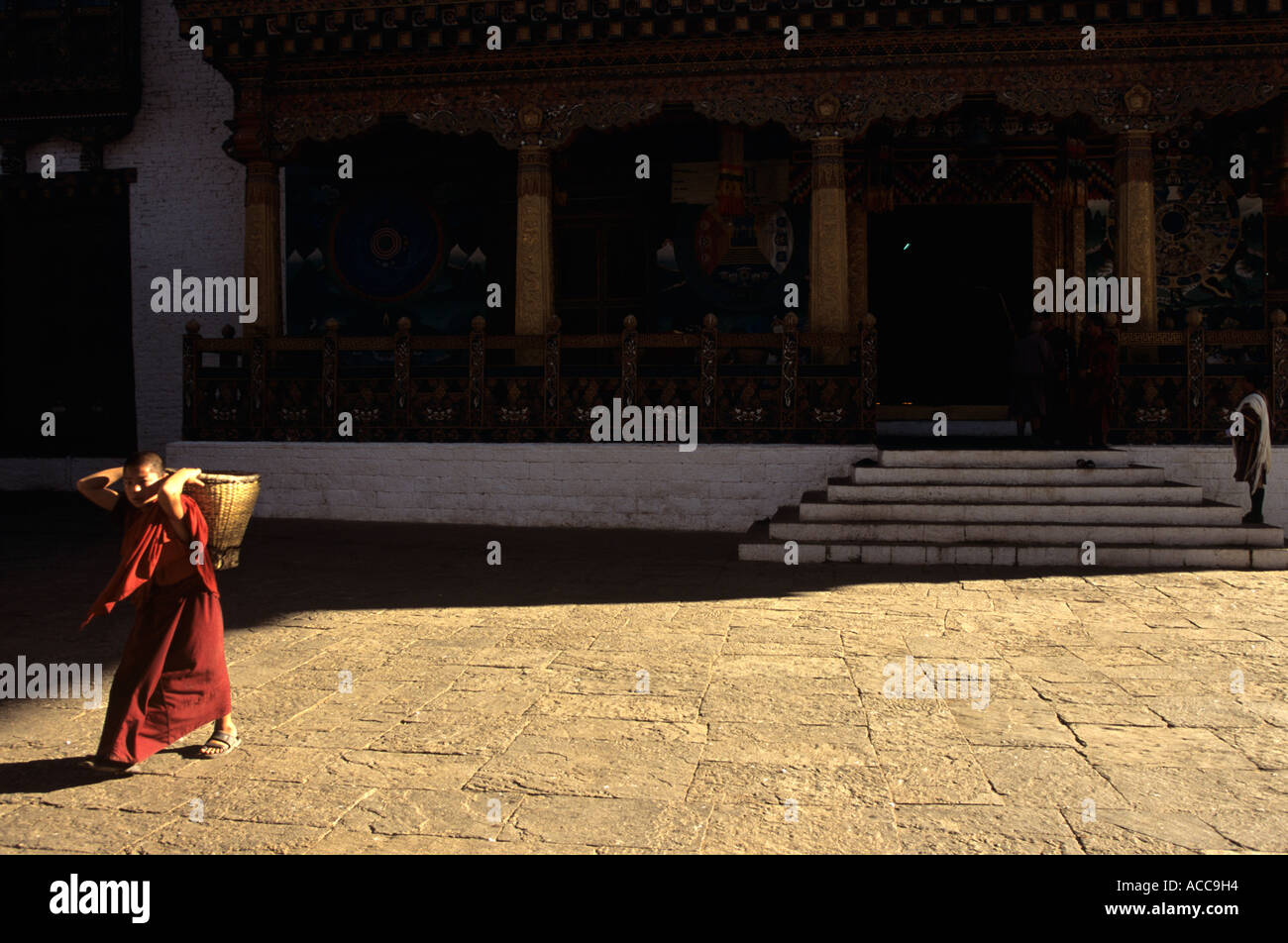 Buddhist monk carrying basket on shoulders in Dzong courtyard, Bhutan ...
