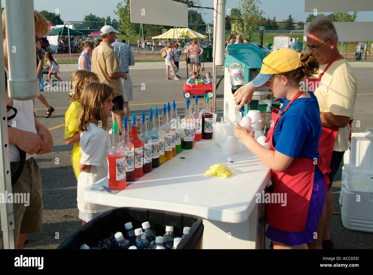 Vendor sells flavored snow cones to adults and children at a carnival ...