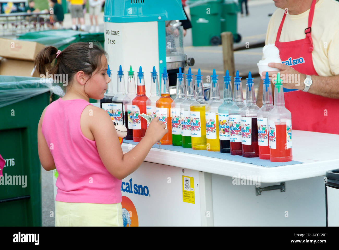 Vendor sells flavored snow cones to adults and children at a carnival ...