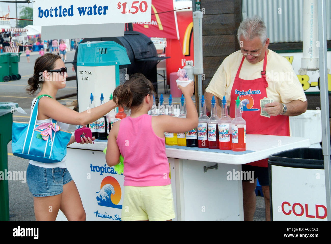 Vendor sells flavored snow cones to adults and children at a carnival ...