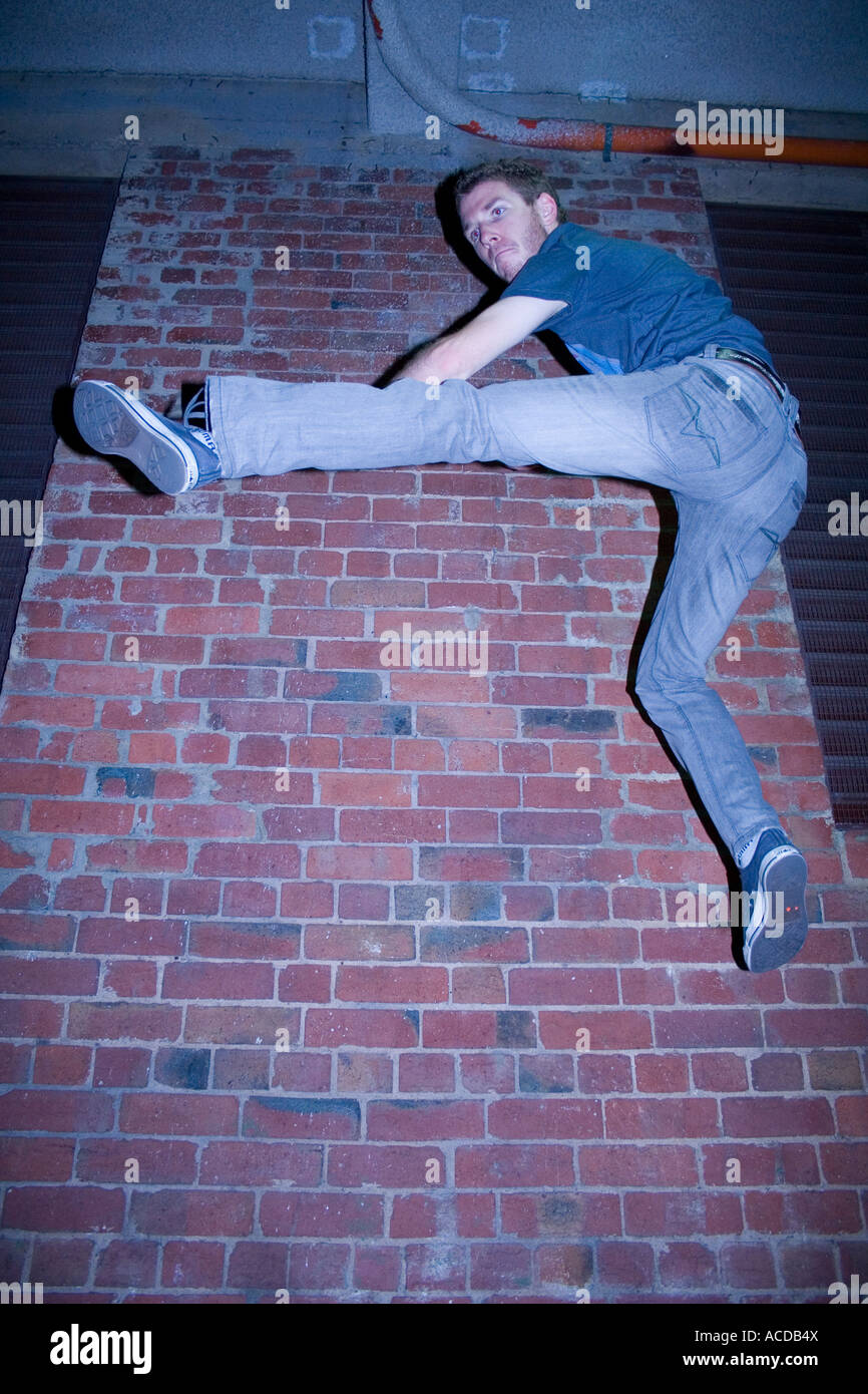 young male man teenager kicking flying in air against brick wall ...