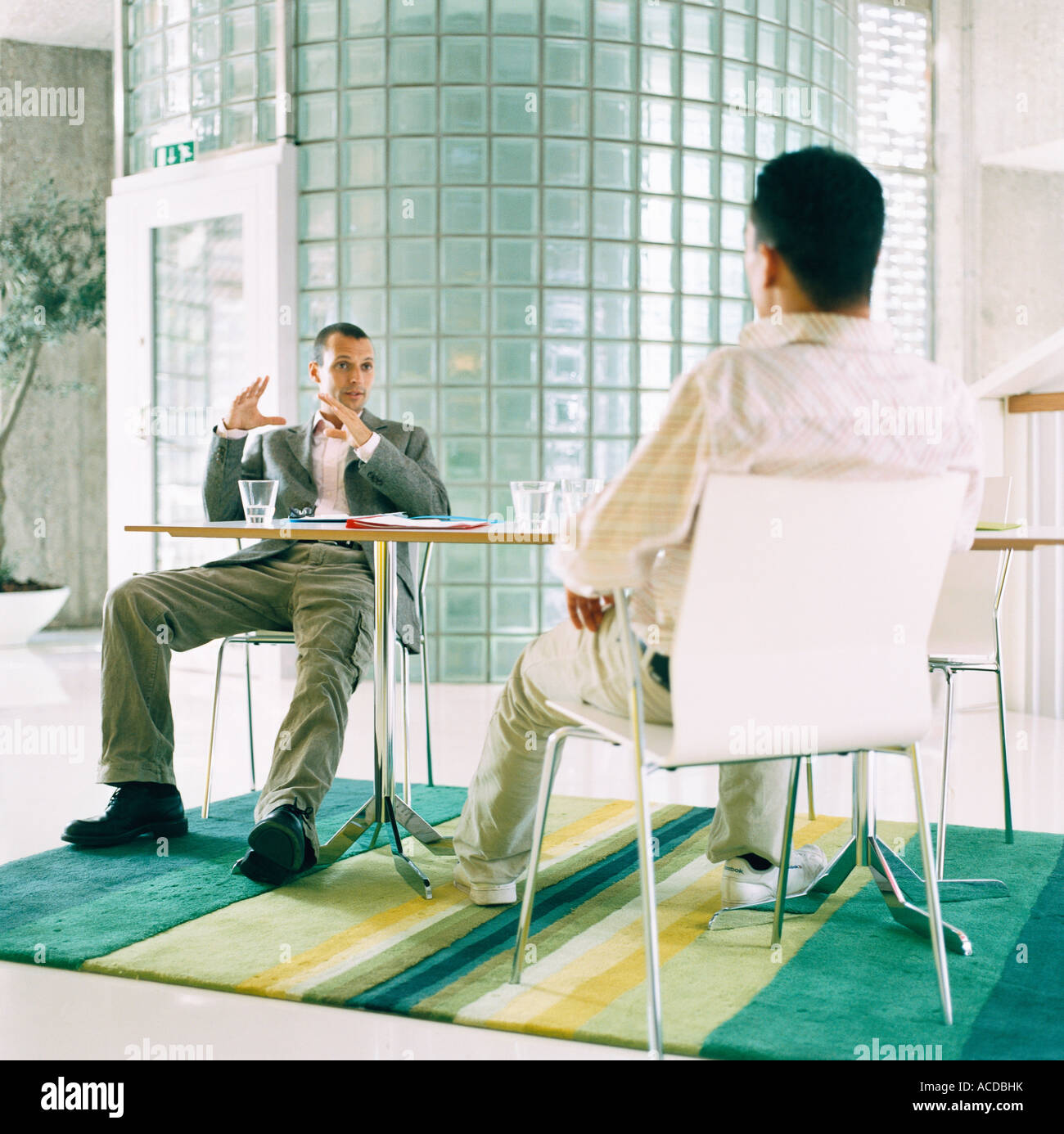Two men conversing sitting by a table in an office environment Stock ...