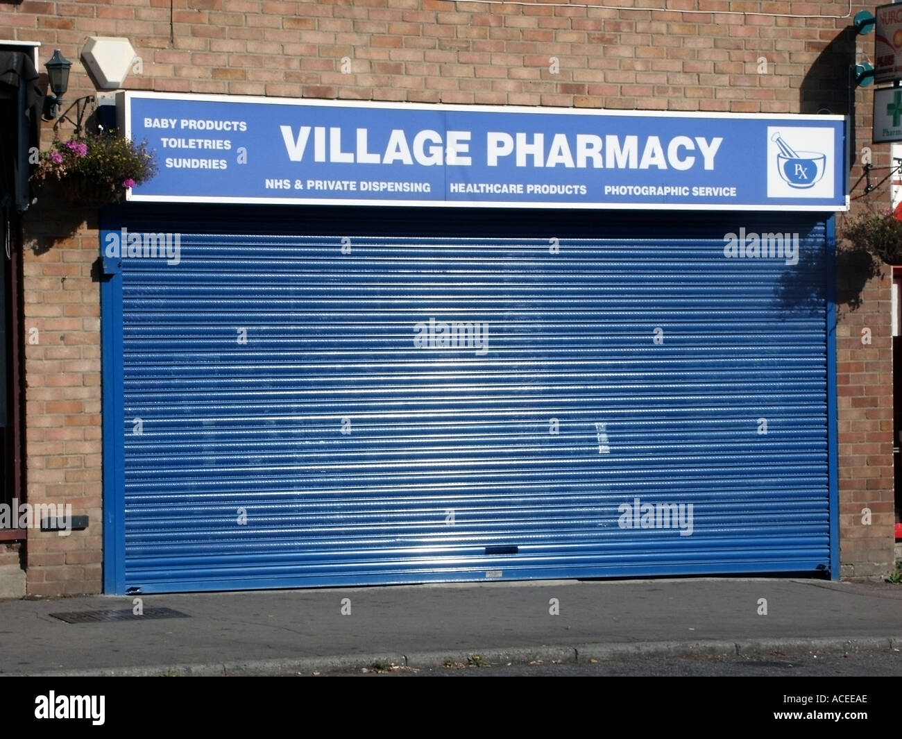 Essex village pharmacy with steel roller shutter protecting shop front ...