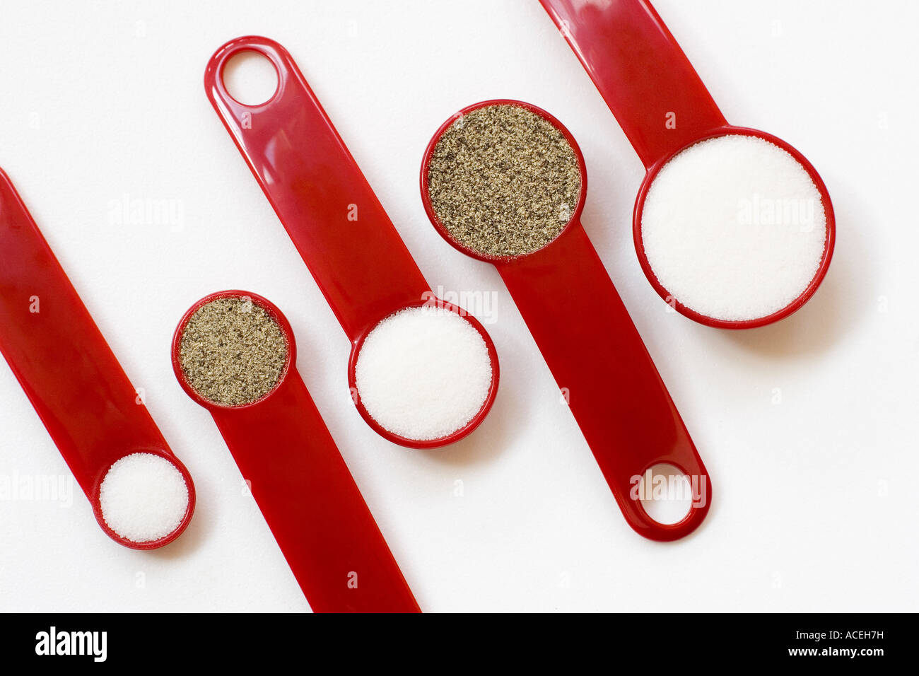 Five red measuring spoons filled with salt and pepper on a white ...