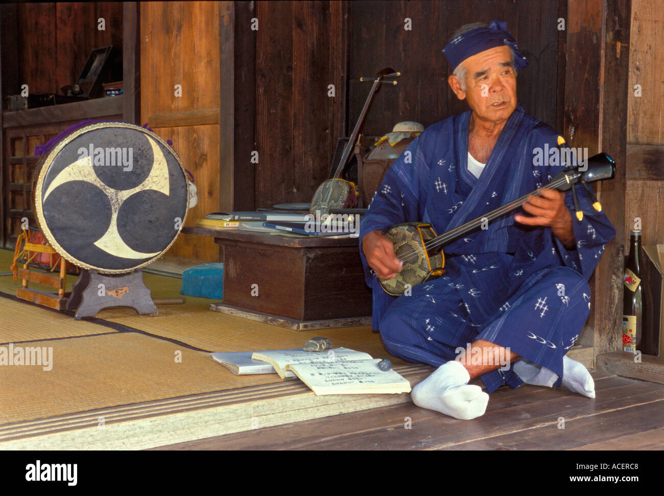 Man wearing traditional costume playing a three string sanshin banjo ...