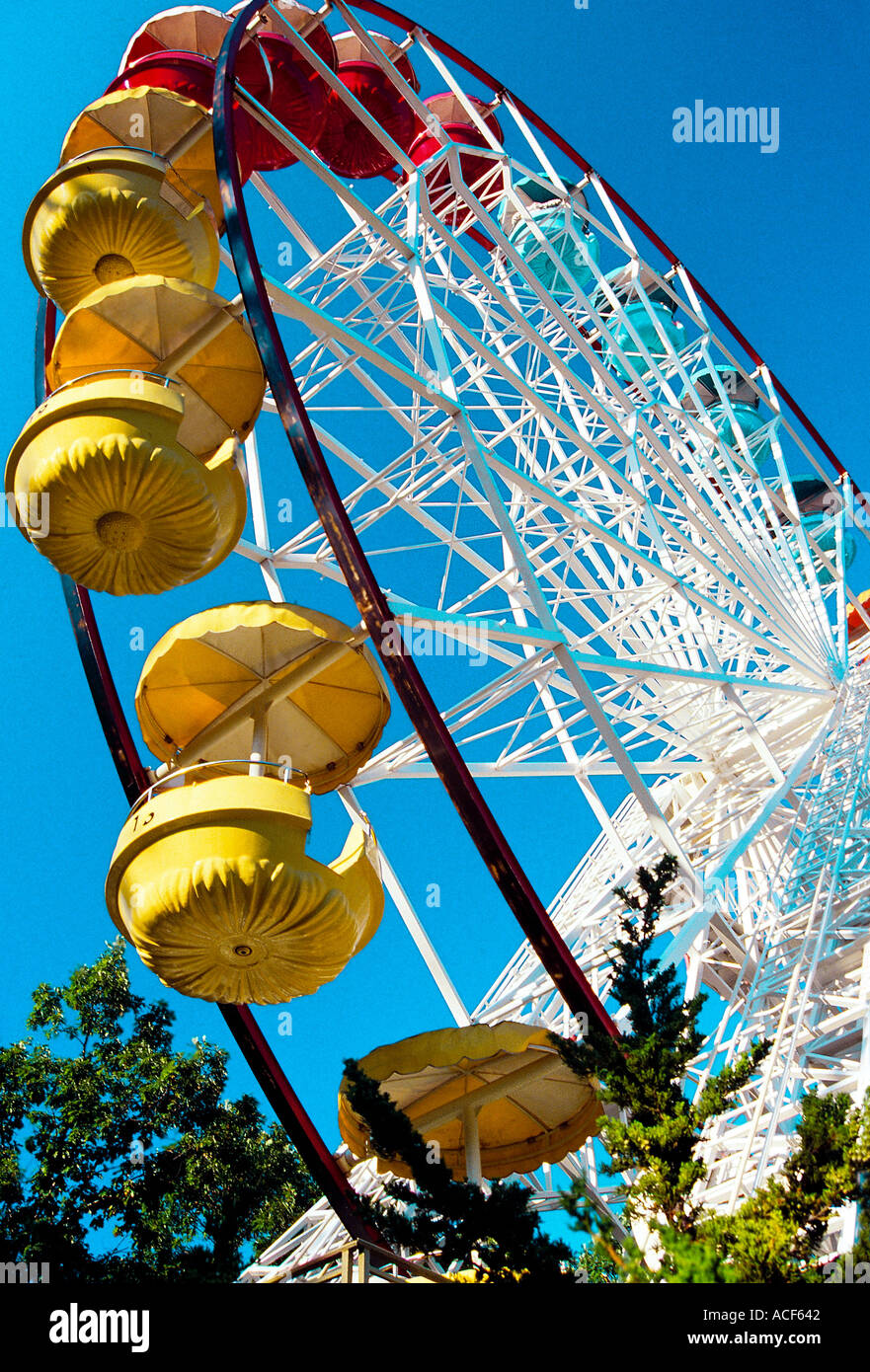 Looking up at a large ferris wheel and its yellow red and blue cars ...