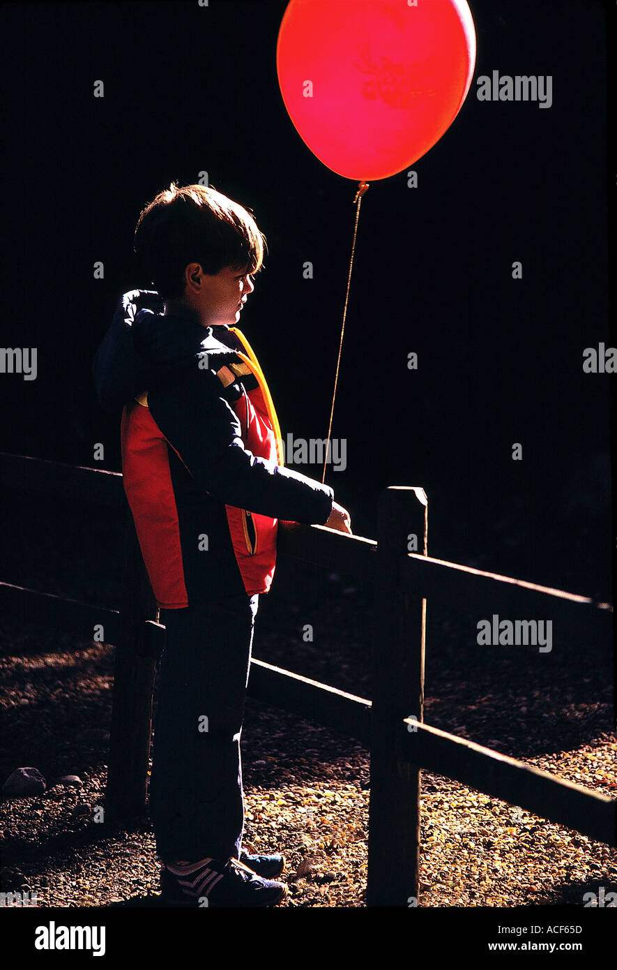 A child stands by a low rail fence and holds a red helium balloon Stock ...