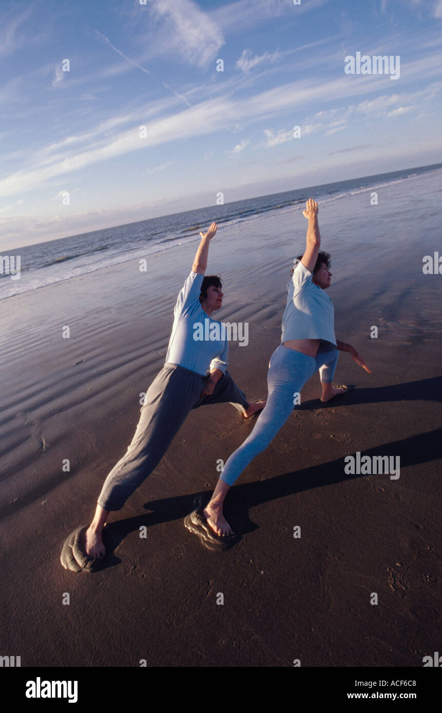Two women synchronize their yoga stretching exercises on the beach at ...