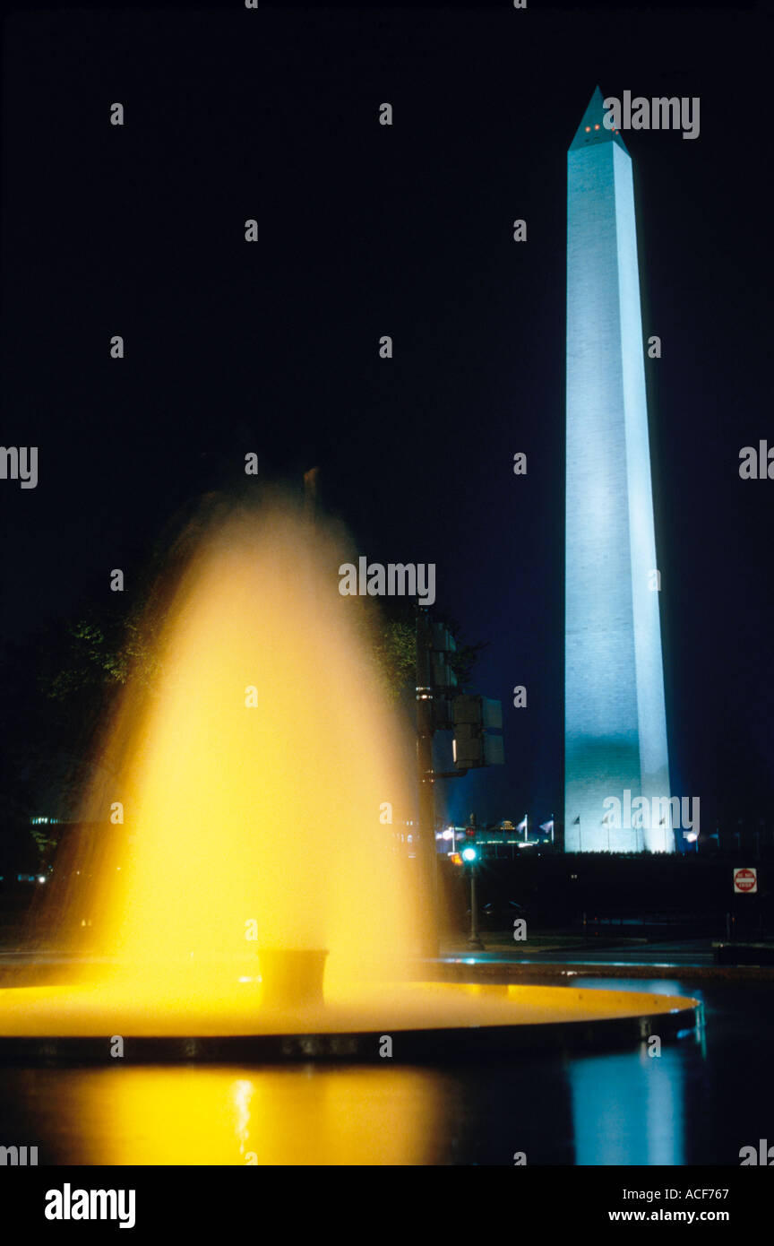 Washington Monument illuminated at night rises behind a fountain lit by ...