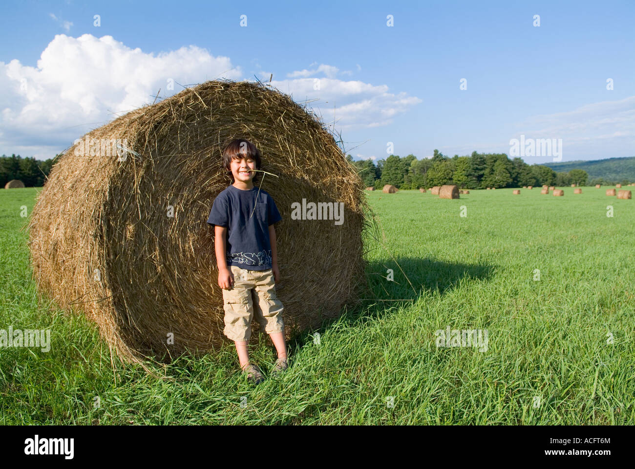 Young boy with straw in his mouth making funny face leaning on hay bale ...