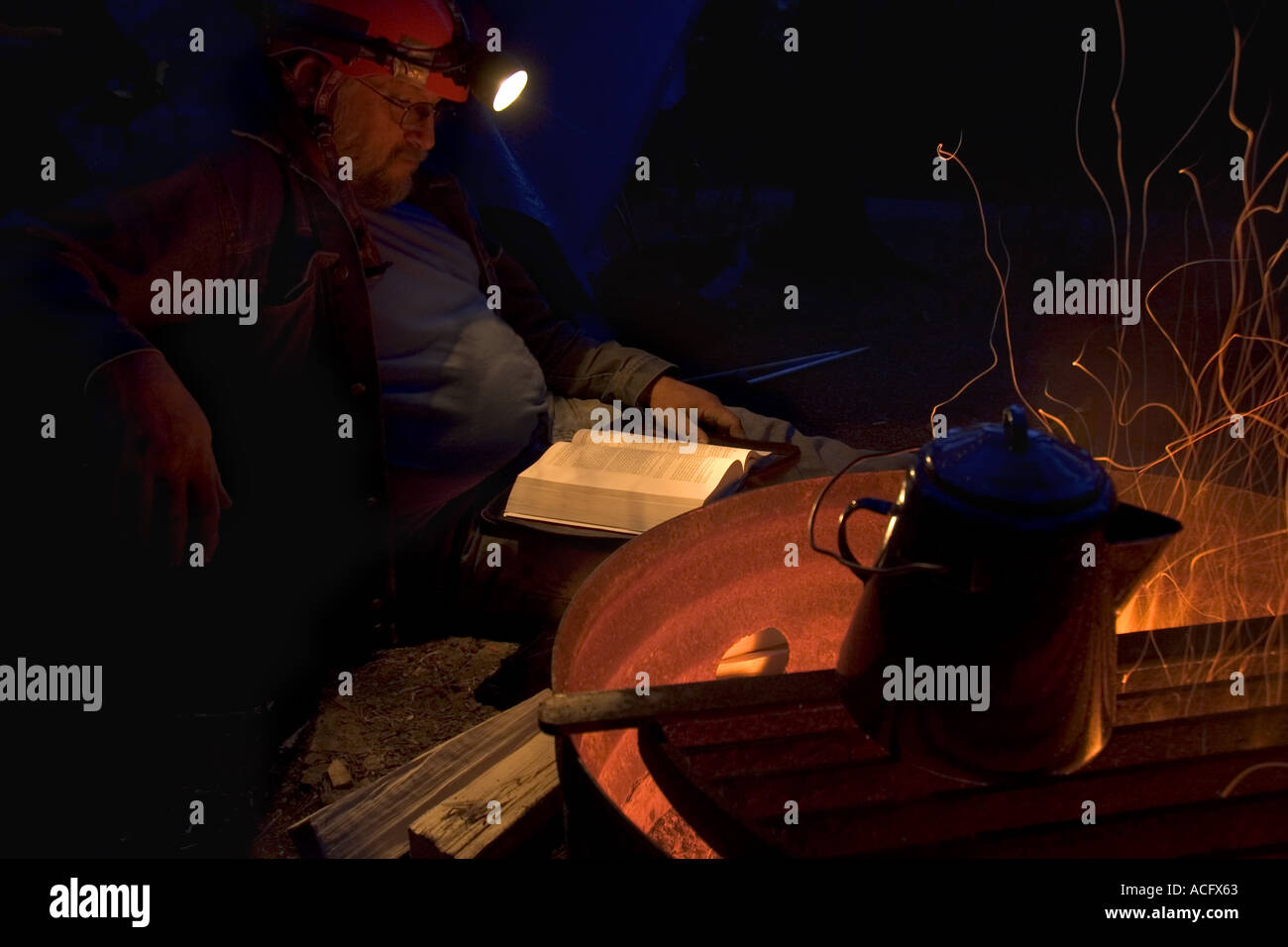 Man reading Bible at night next to fire Stock Photo - Alamy