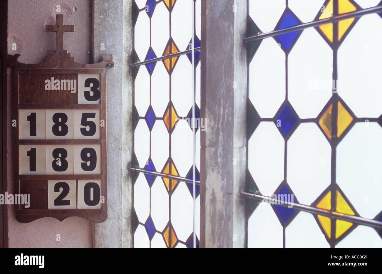 Board indicating selected hymn numbers hanging on pink wall next to ...