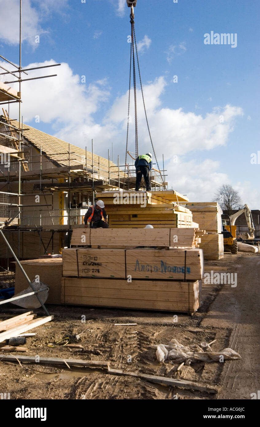Construction workers handling timber by crane sling on building site ...