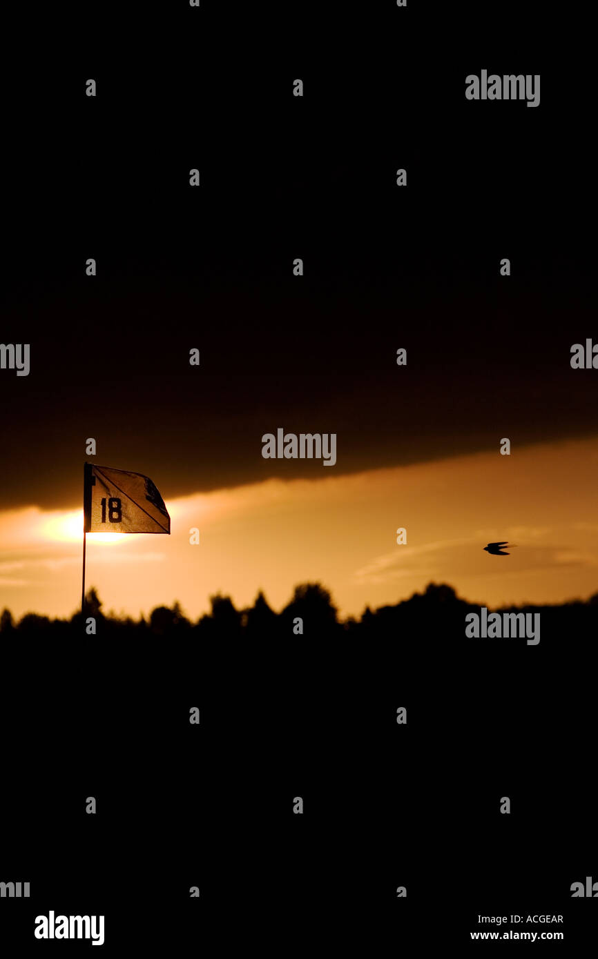 Golf course 18th hole flag silhouette against a sun setting behind a ...