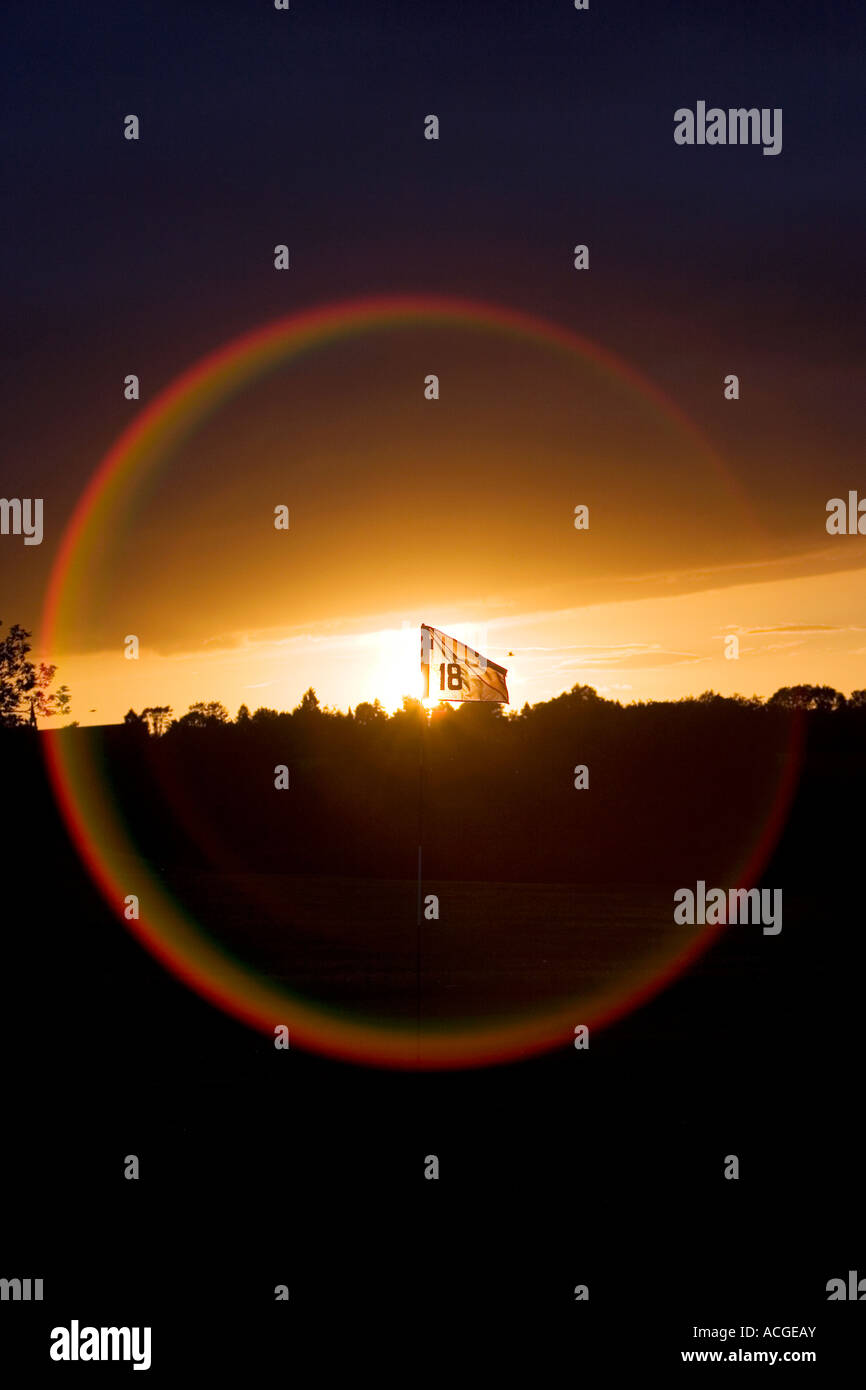 Golf course 18th hole flag silhouette against a sun setting behind a ...