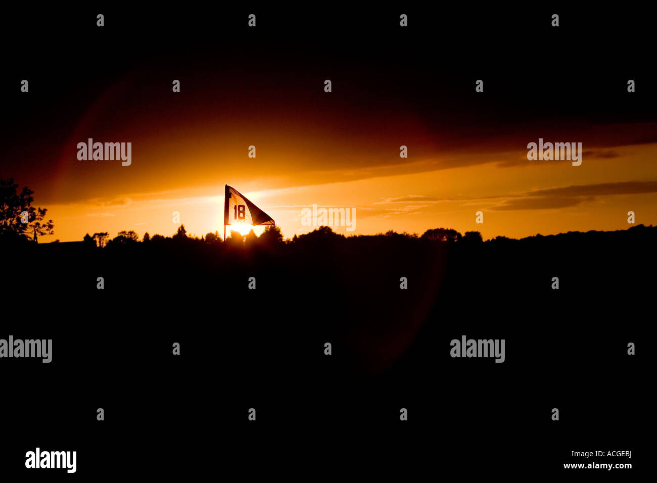Golf course 18th hole flag silhouette against a sun setting behind a ...