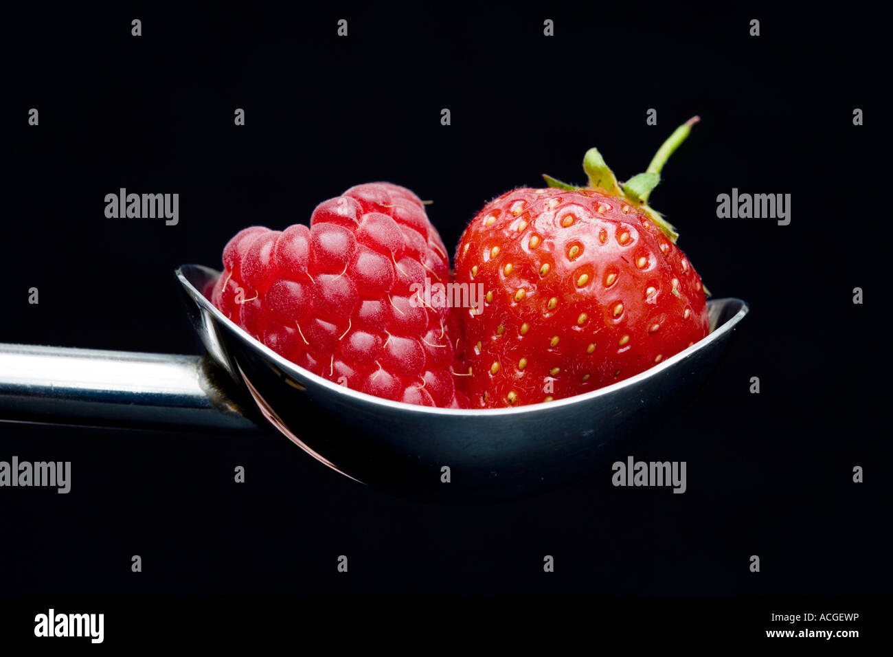 Raspberry and Strawberry in a scoop spoon against black background ...