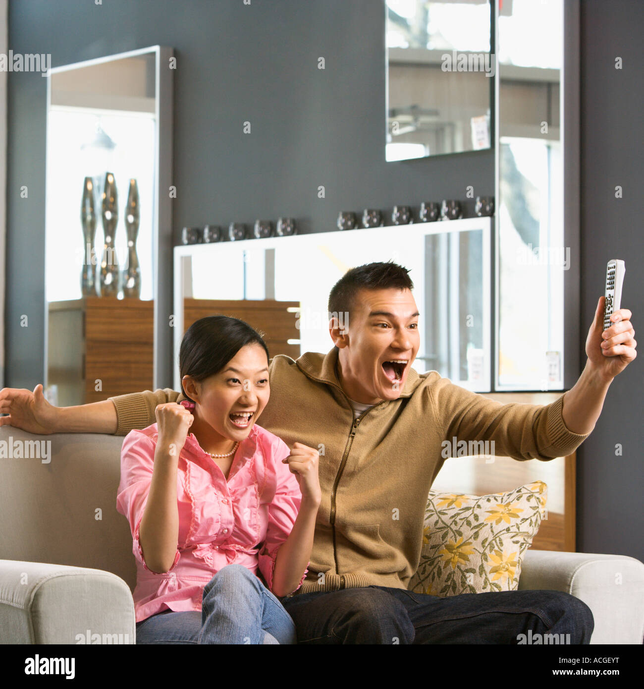 Asian couple cheering while watching television Stock Photo - Alamy