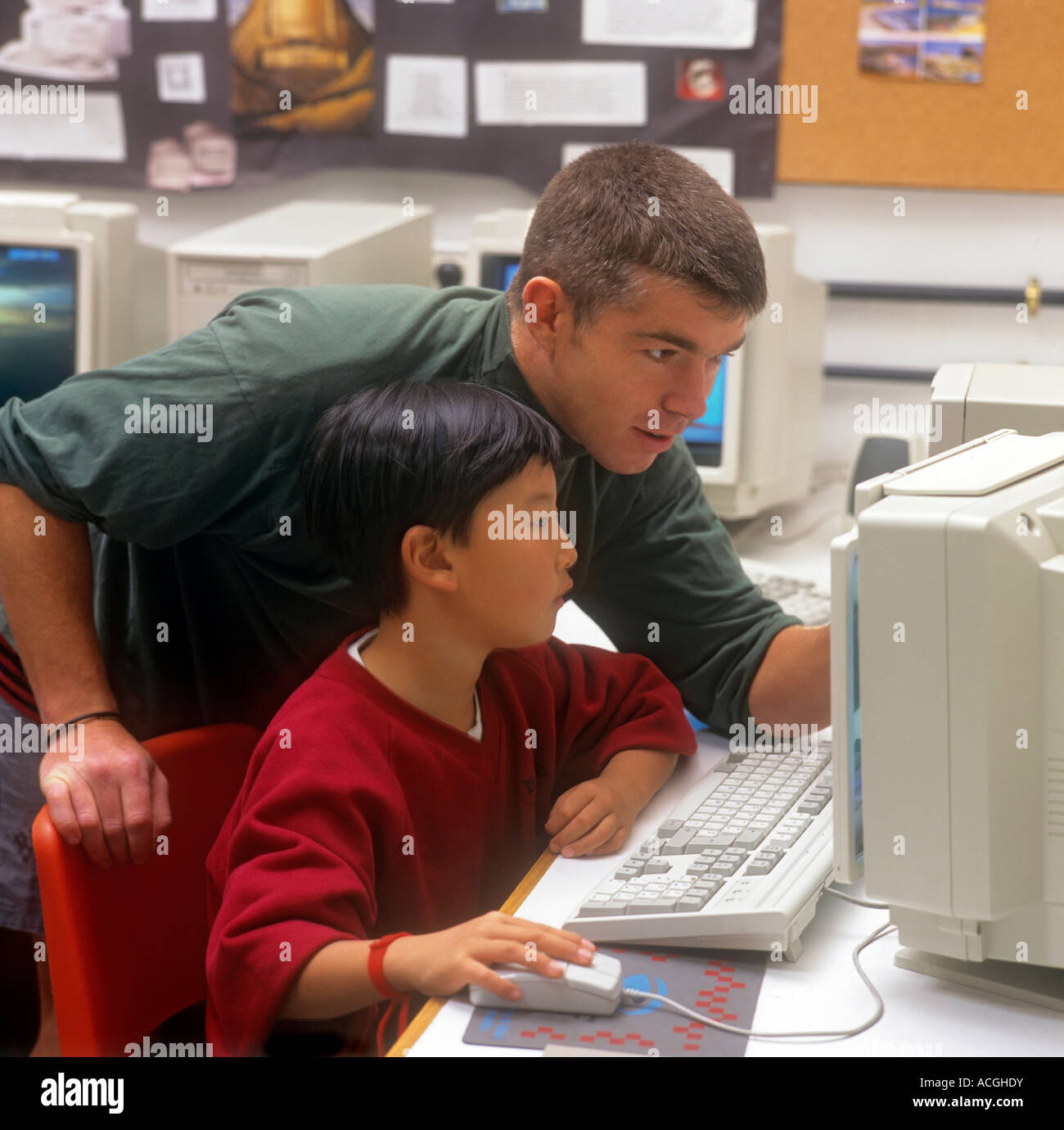 Teacher and junior oriental schoolboy studying together at a computer ...
