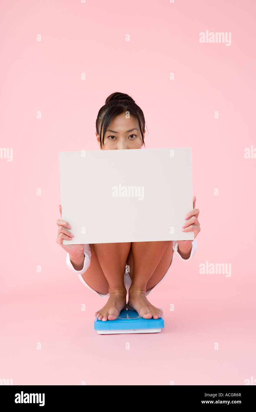 Woman crouching on bathroom scale holding blank placard Stock Photo - Alamy